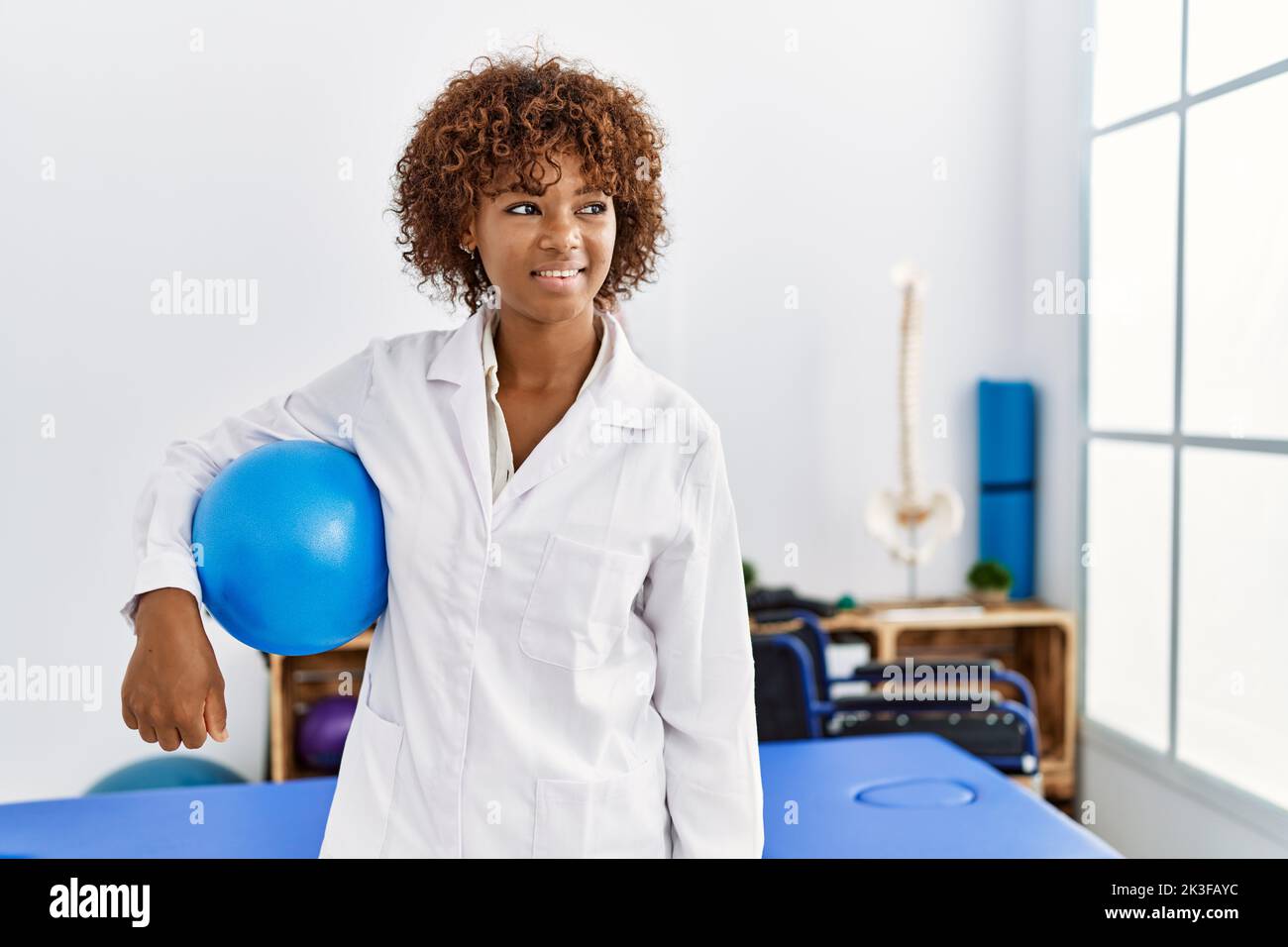 Young african american woman wearing physio uniform holding fit ball at ...