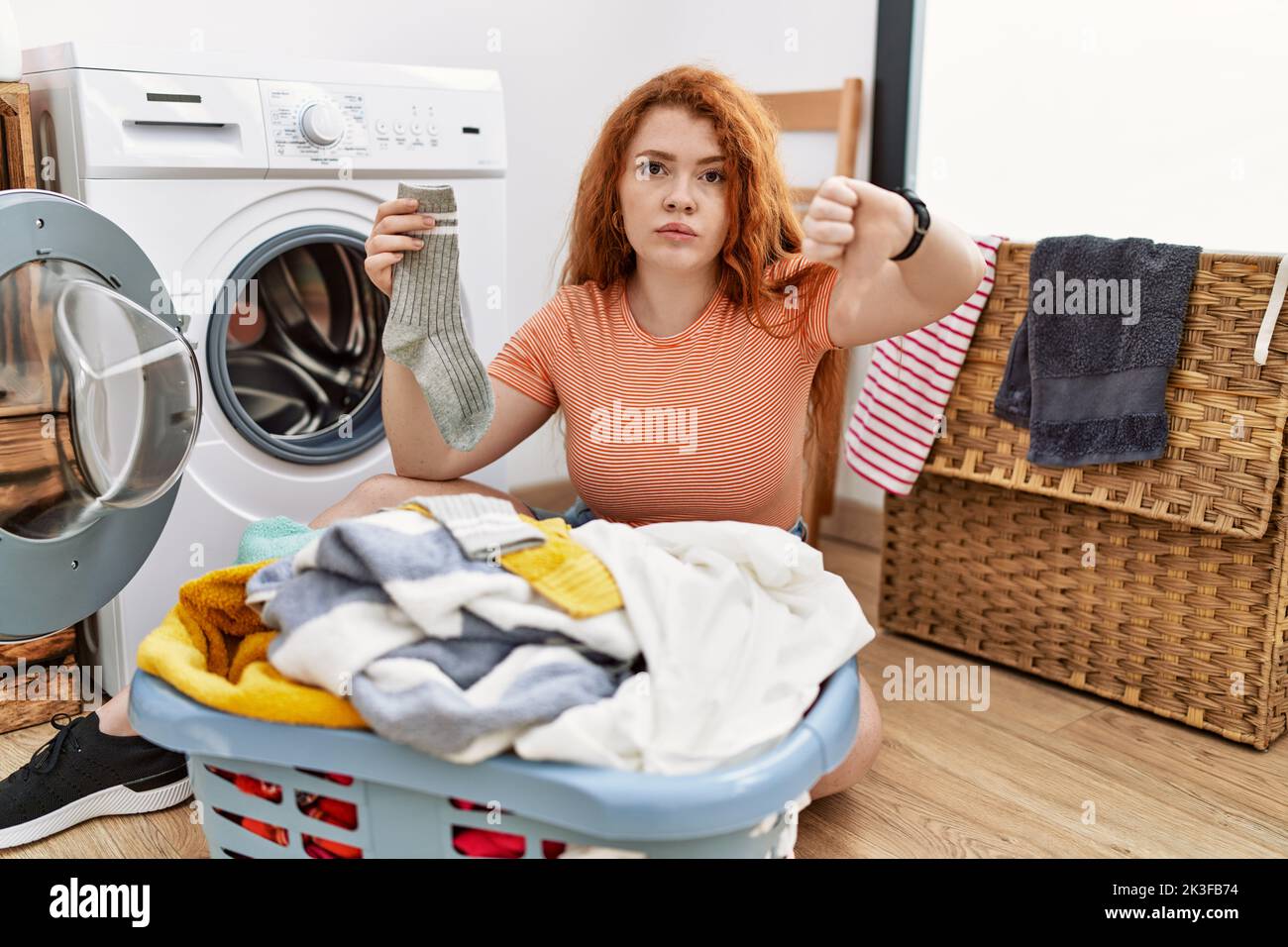 Young redhead woman putting dirty laundry into washing machine looking ...