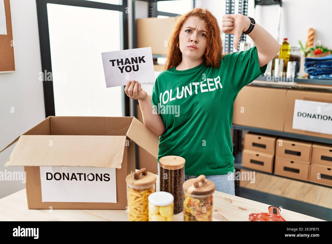 Young redhead woman wearing volunteer t shirt holding thank you banner ...