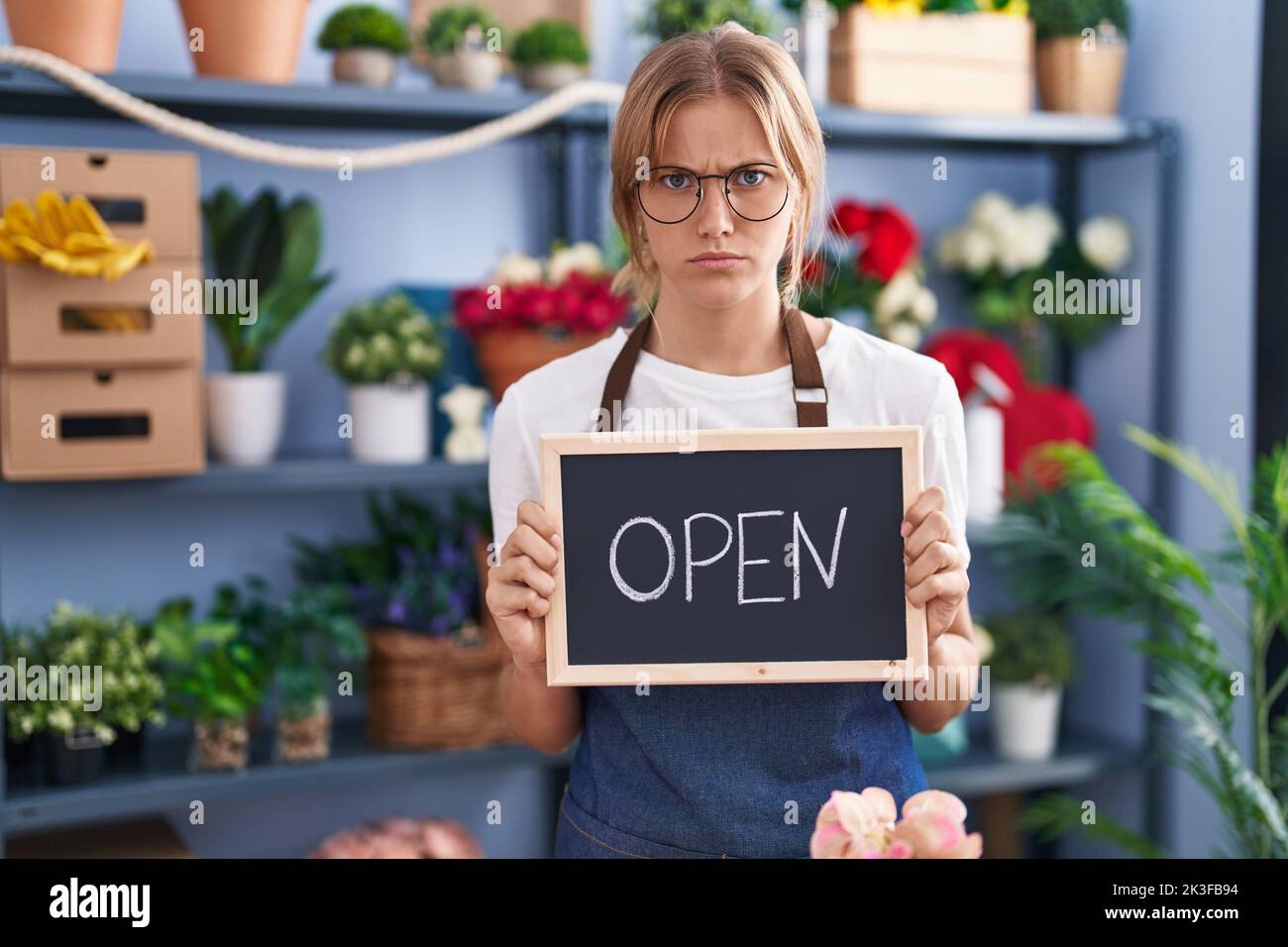 Young caucasian woman working at florist with open sign skeptic and ...
