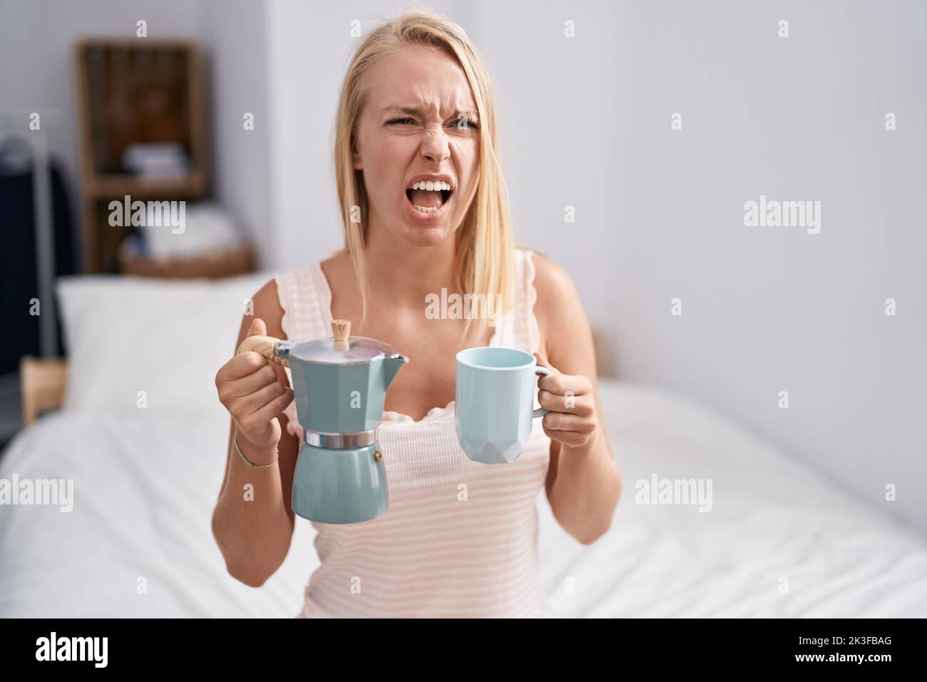 Young caucasian woman drinking coffee on the bed angry and mad ...