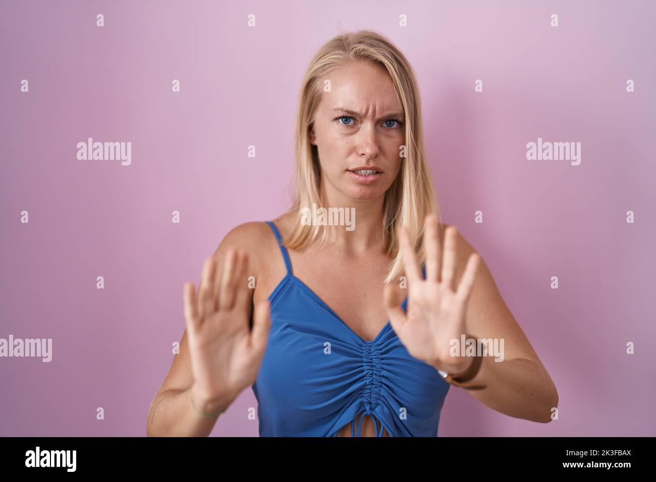 Young caucasian woman standing over pink background moving away hands ...