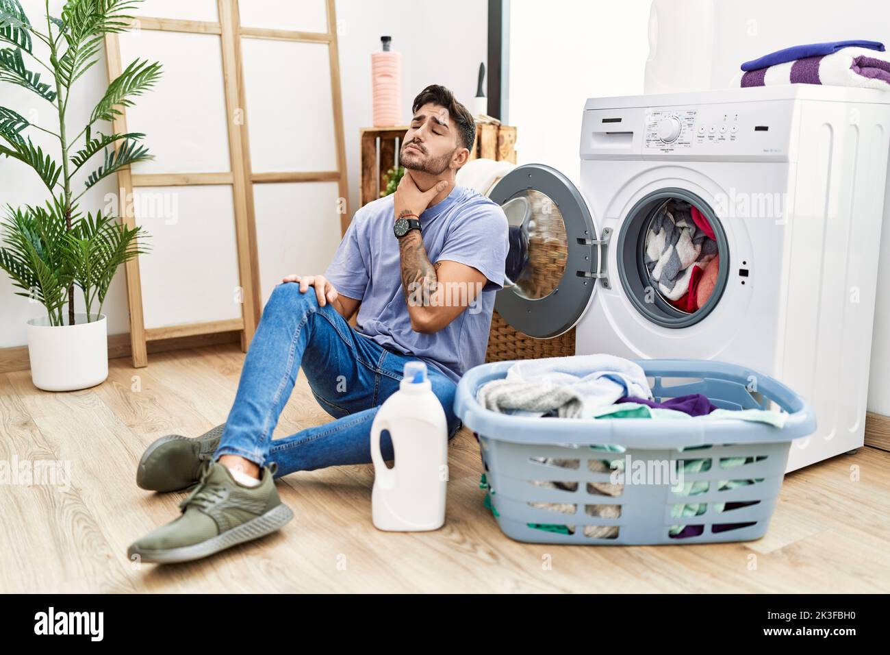 Young hispanic man putting dirty laundry into washing machine touching ...