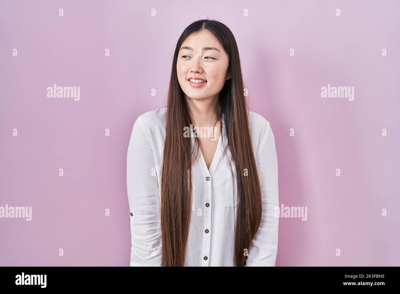 Chinese young woman standing over pink background looking away to side ...