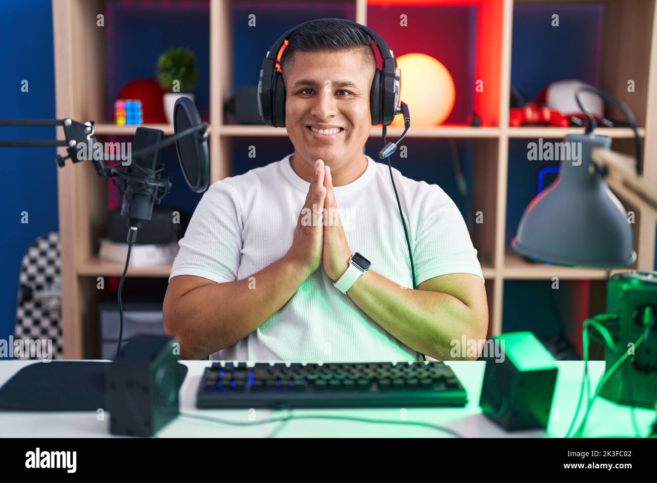Young hispanic man playing video games praying with hands together ...