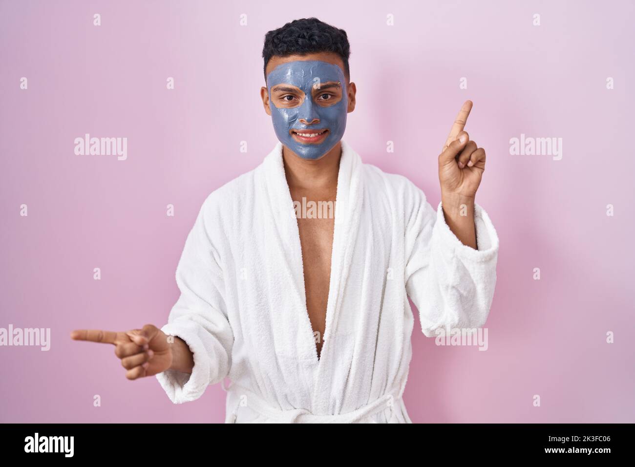 Young hispanic man wearing beauty face mask and bath robe smiling ...