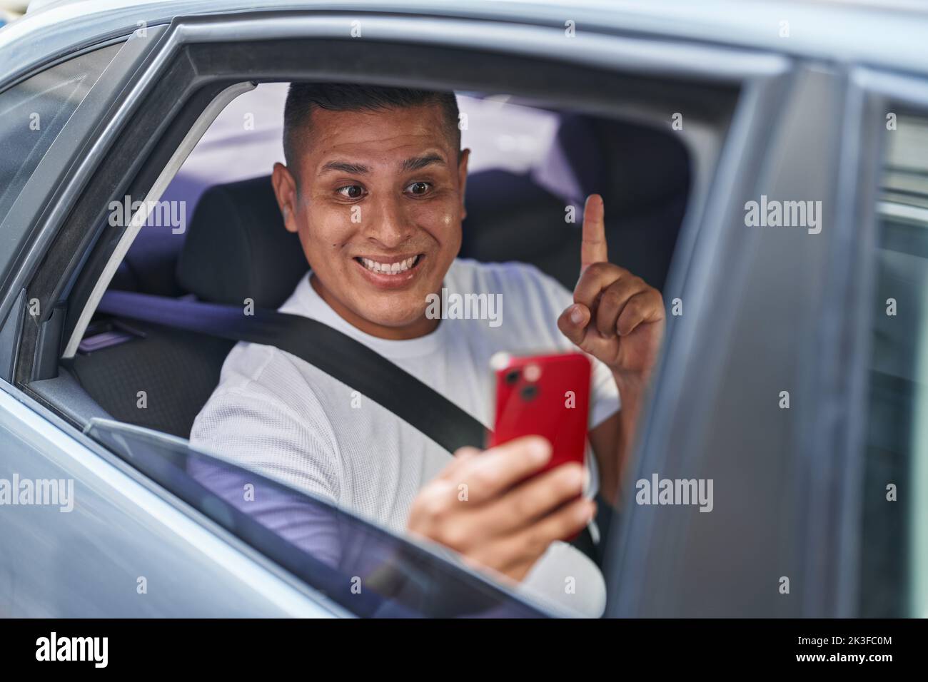 Young hispanic man doing video call with smartphone in the car smiling ...