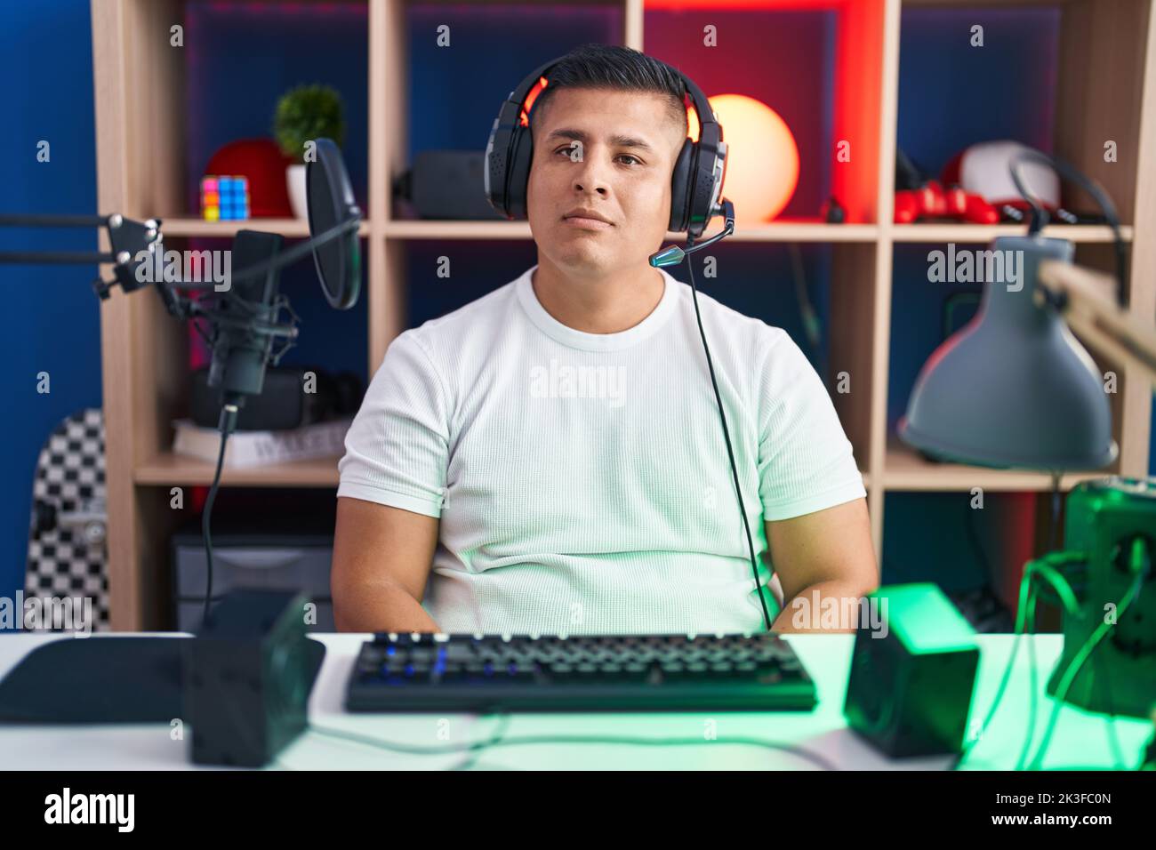 Young hispanic man playing video games relaxed with serious expression ...