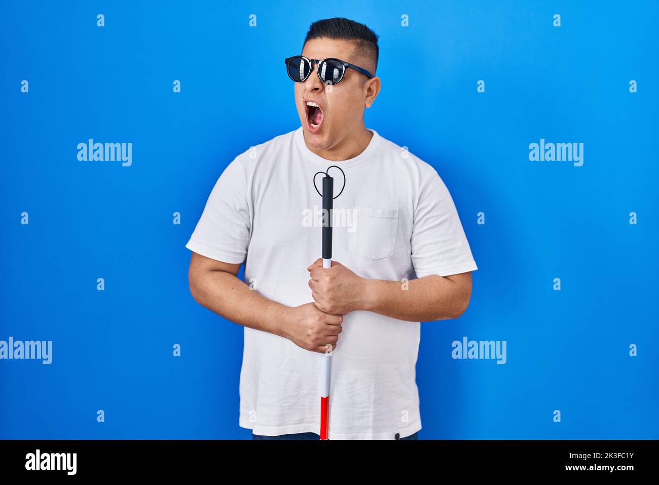 Hispanic young blind man holding cane angry and mad screaming ...
