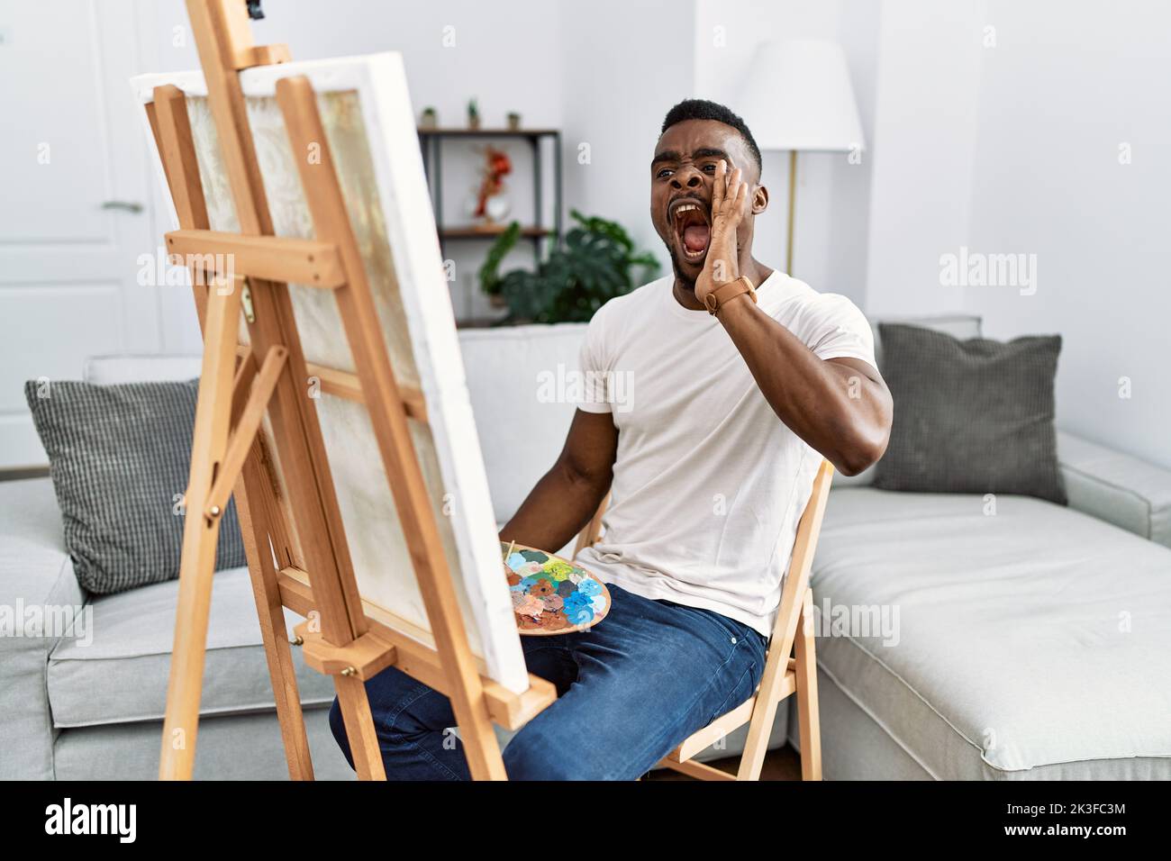 Young african man painting on canvas at home shouting and screaming ...