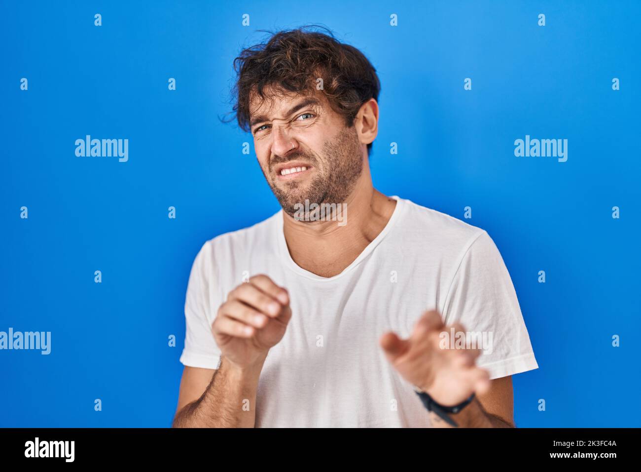 Hispanic young man standing over blue background disgusted expression ...