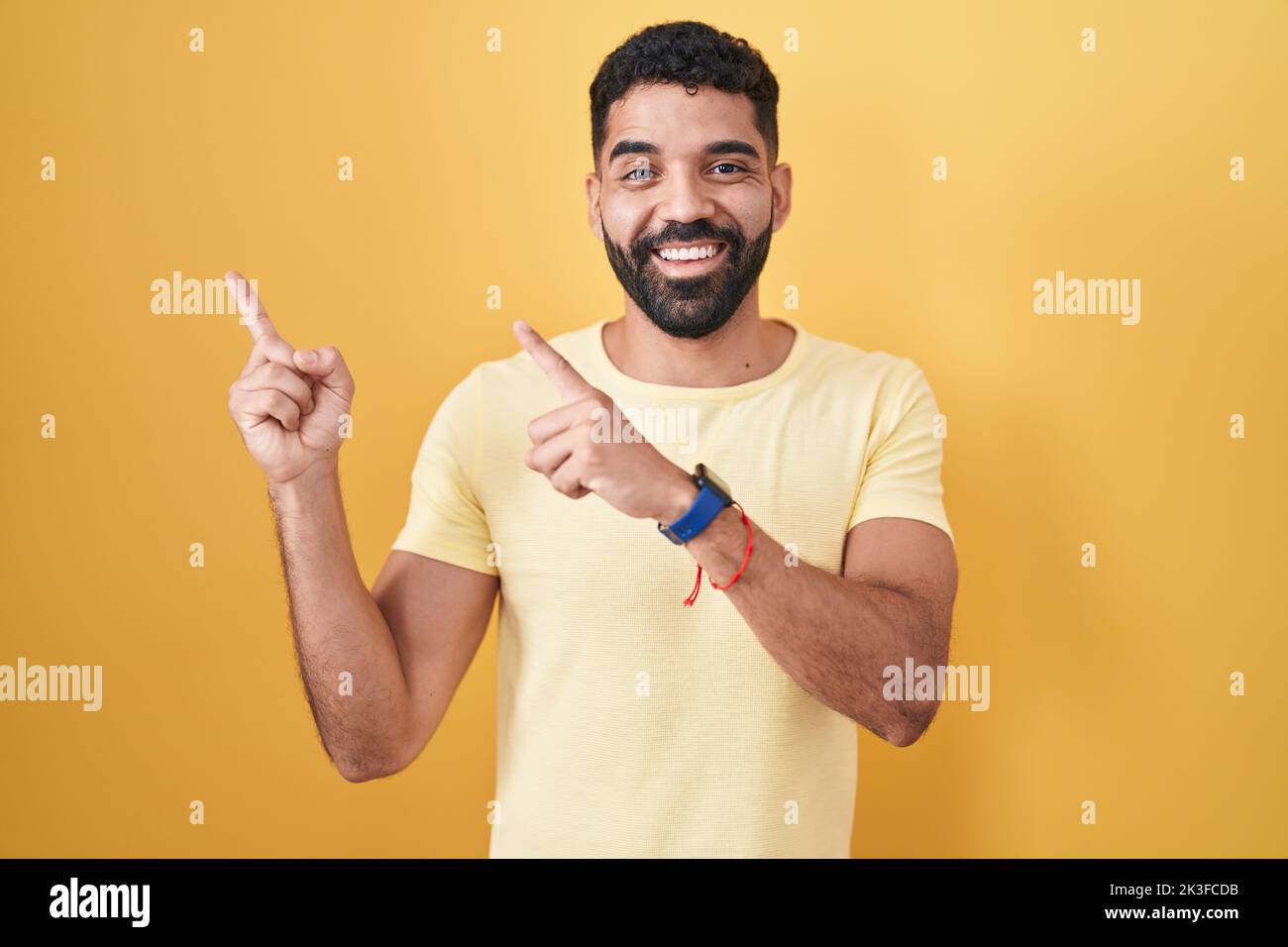 Hispanic man with beard standing over yellow background smiling and ...