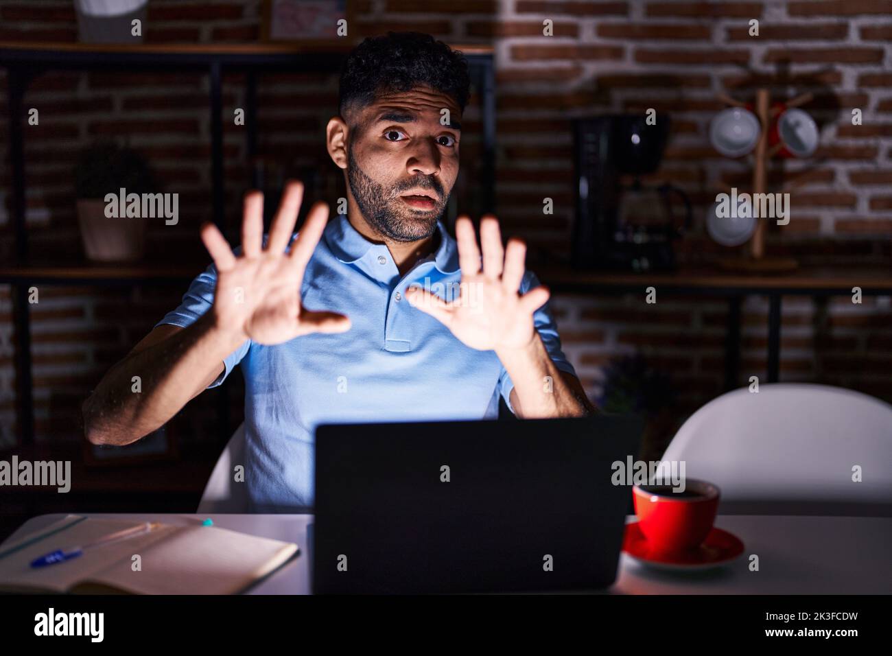 Hispanic man with beard using laptop at night afraid and terrified with ...