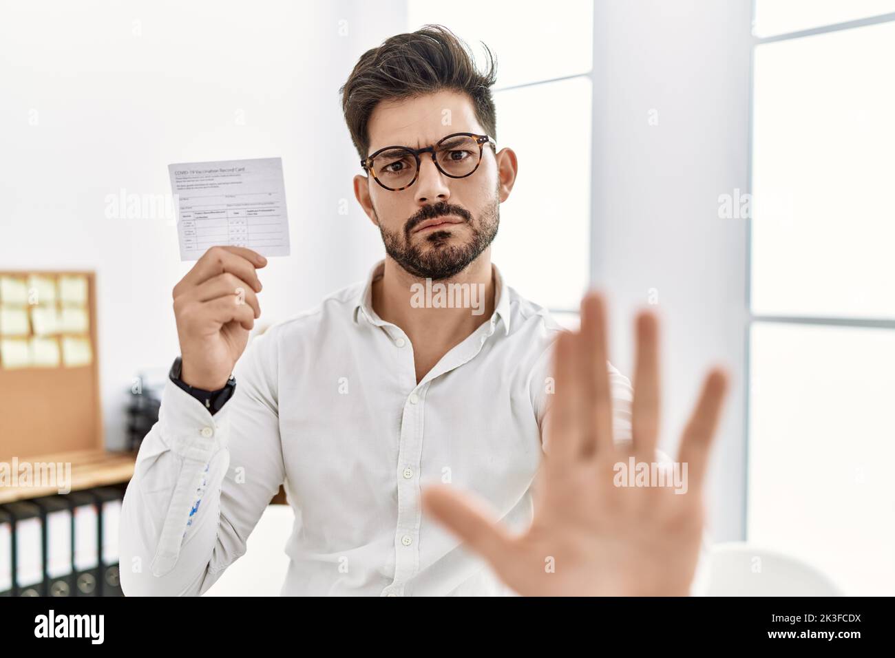 Young man with beard holding covid record card with open hand doing ...