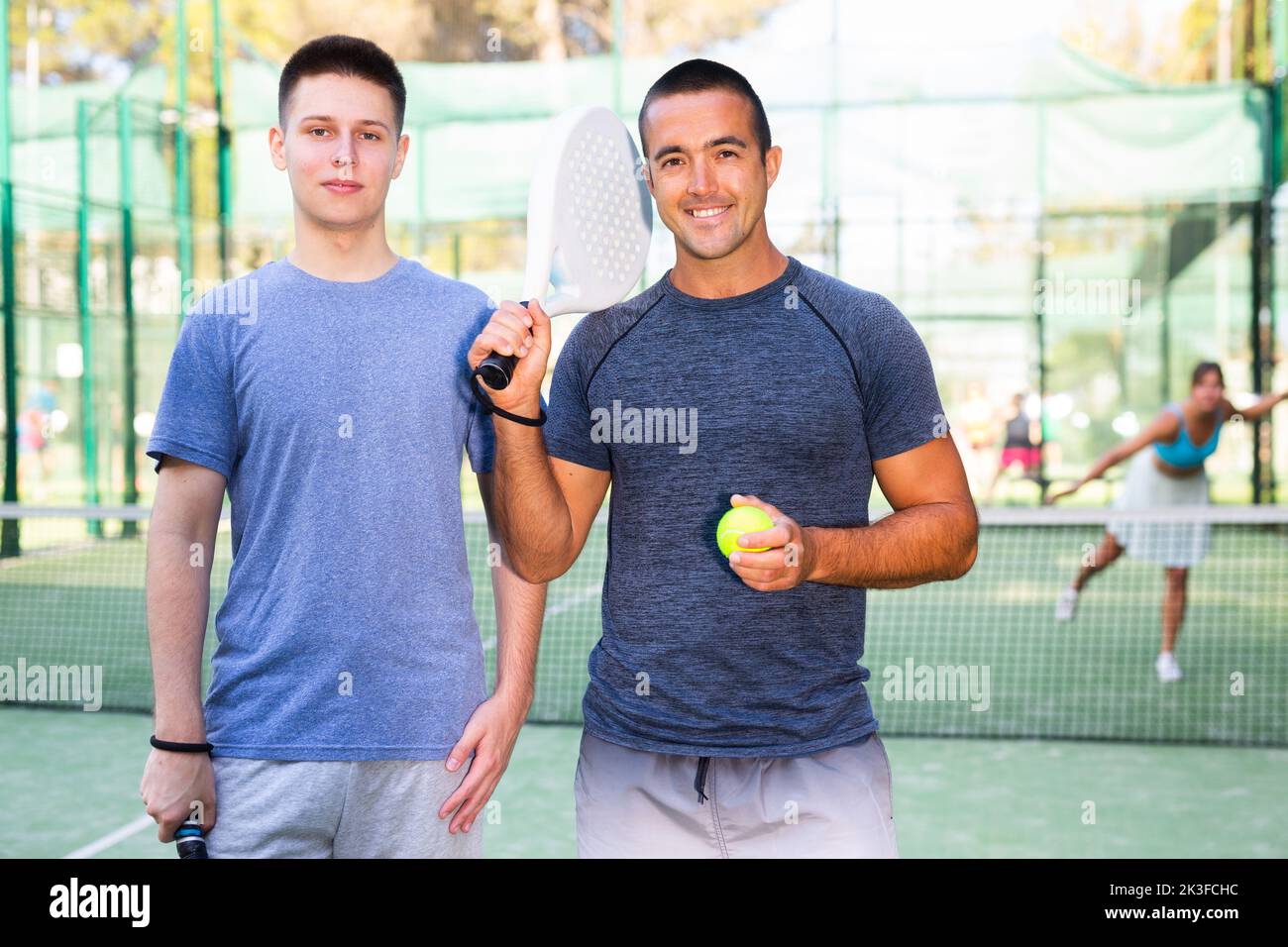 Smiling man standing with teenage son on outdoor tennis court Stock ...