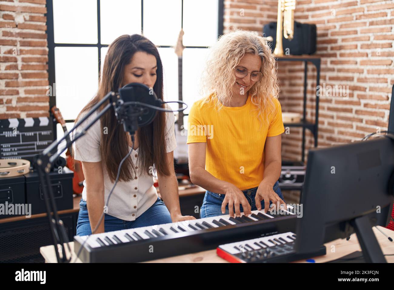 Two women musicians singing song playing piano keyboard at music studio ...