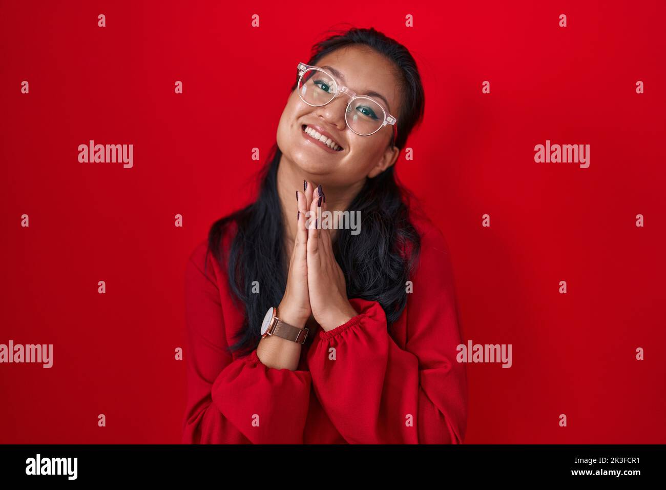 Asian young woman standing over red background praying with hands ...