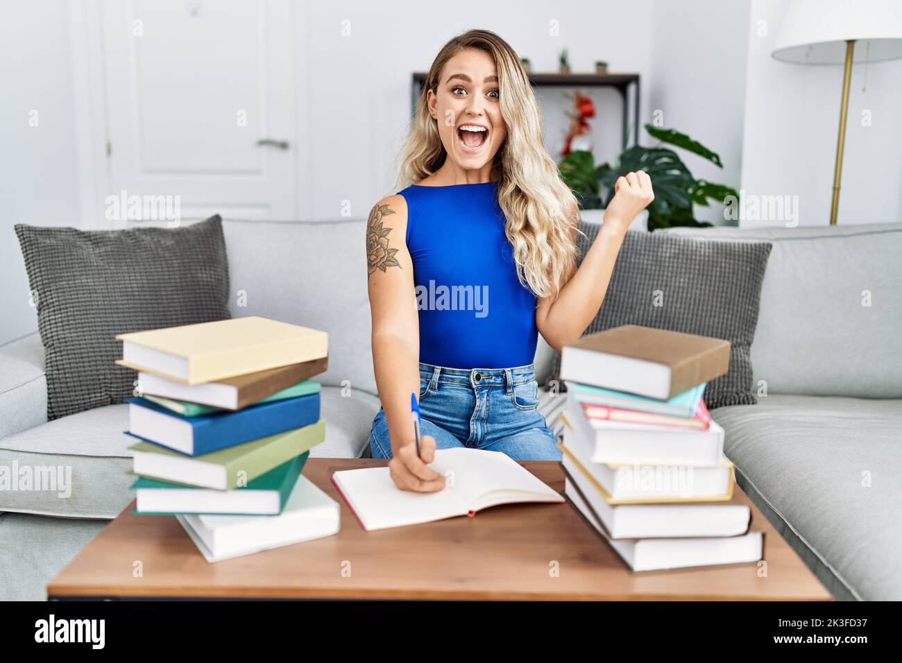 Young beautiful woman writing on notebook around university books ...
