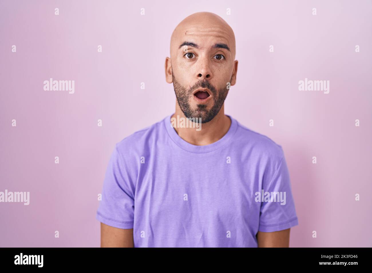 Middle age bald man standing over pink background scared and amazed ...