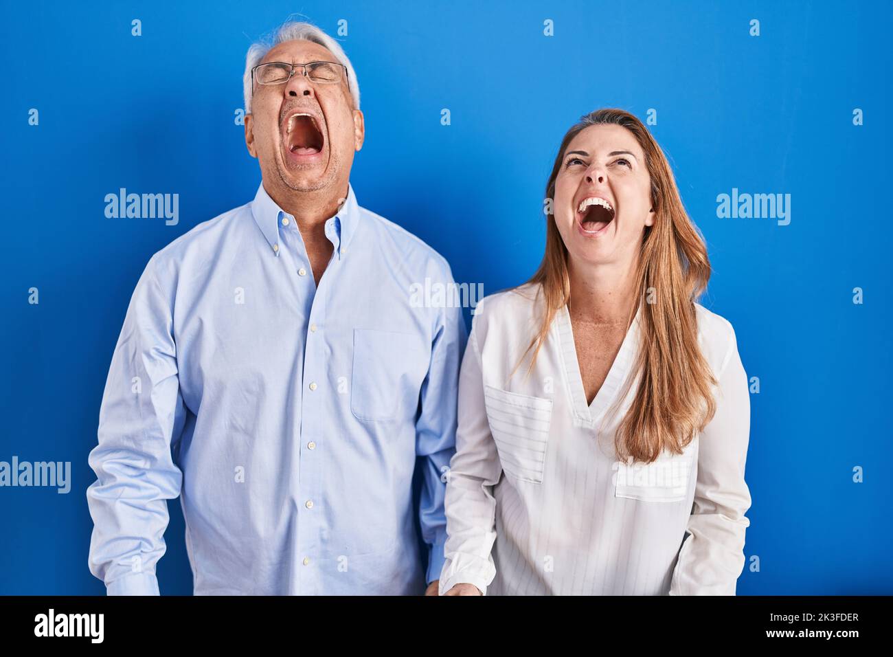 Middle age hispanic couple standing over blue background angry and mad ...