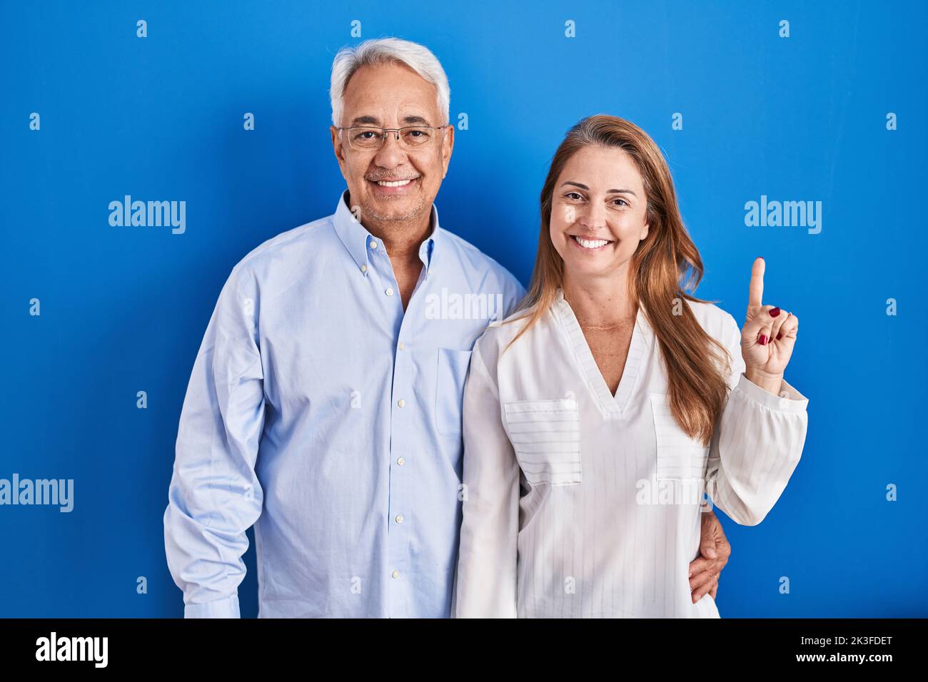 Middle age hispanic couple standing over blue background showing and ...