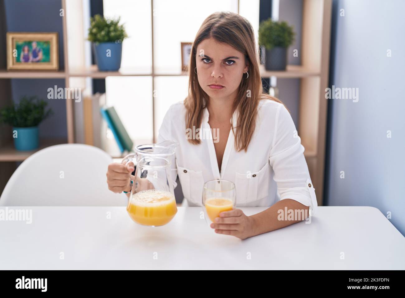 Young hispanic woman drinking glass of orange juice skeptic and nervous ...