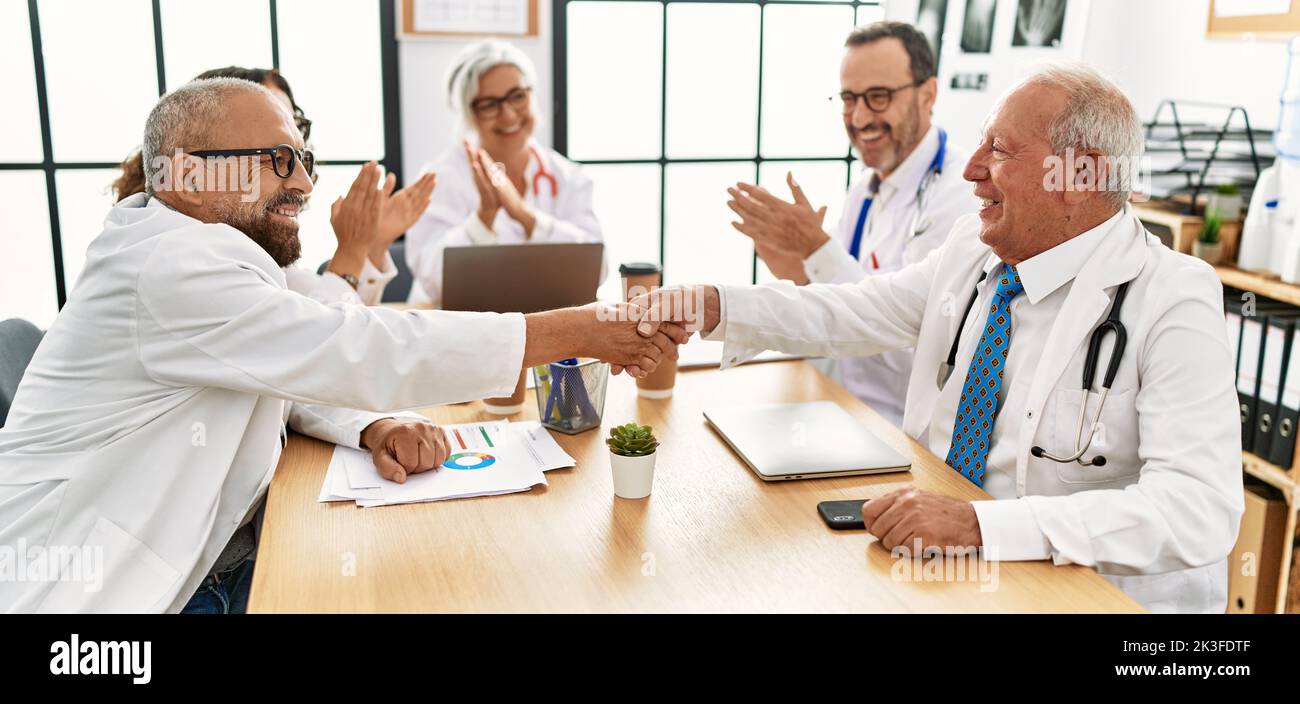Group of middle age doctor smiling and clapping to partners handshake ...