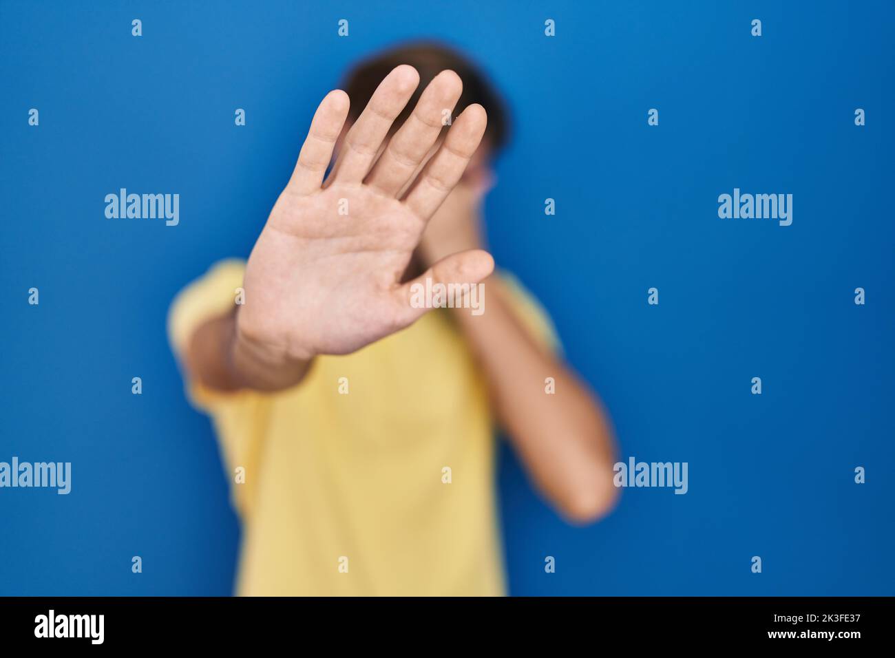 Young man standing over blue background covering eyes with hands and ...