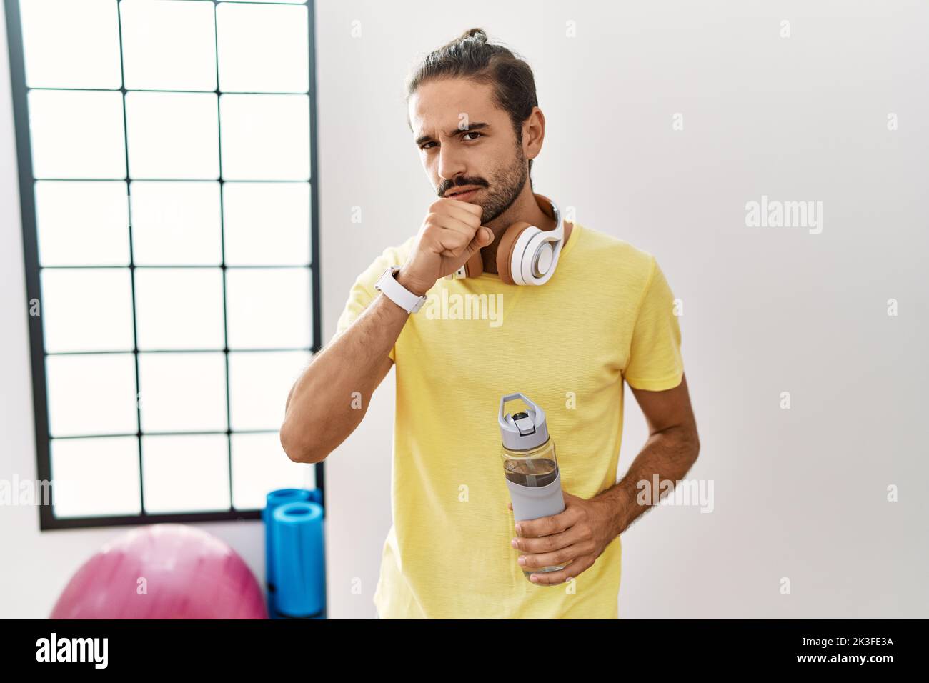 Young hispanic man wearing sportswear and drinking water at the gym ...