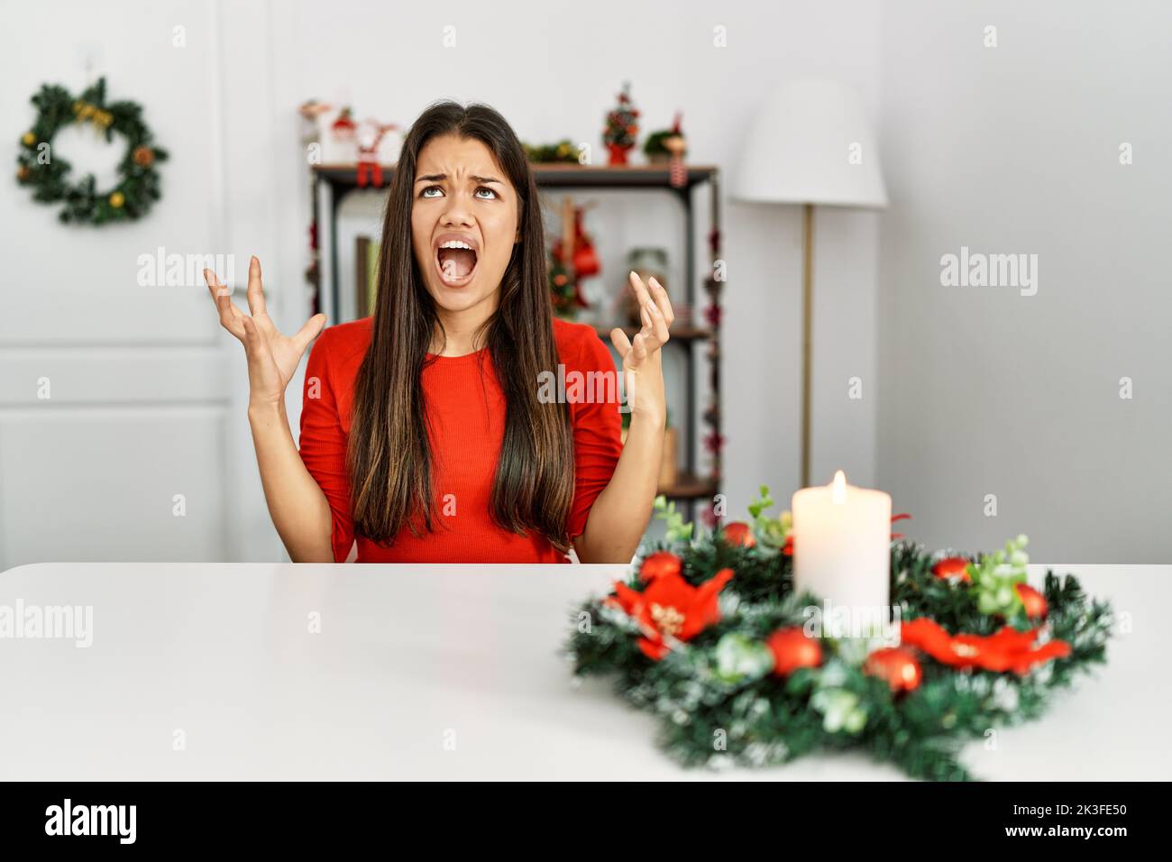 Young brunette woman sitting on the table on christmas crazy and mad ...