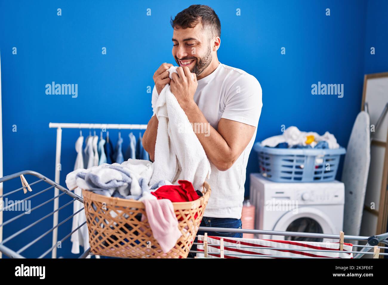 Young hispanic man smelling towel hanging clothes on clothesline at ...