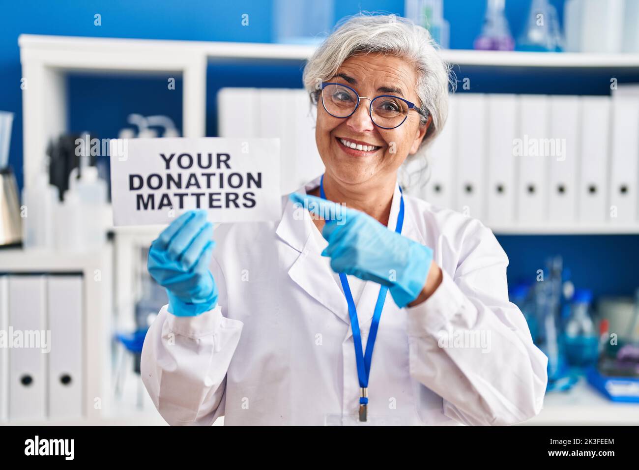 Middle age woman with grey hair working at scientist laboratory holding ...
