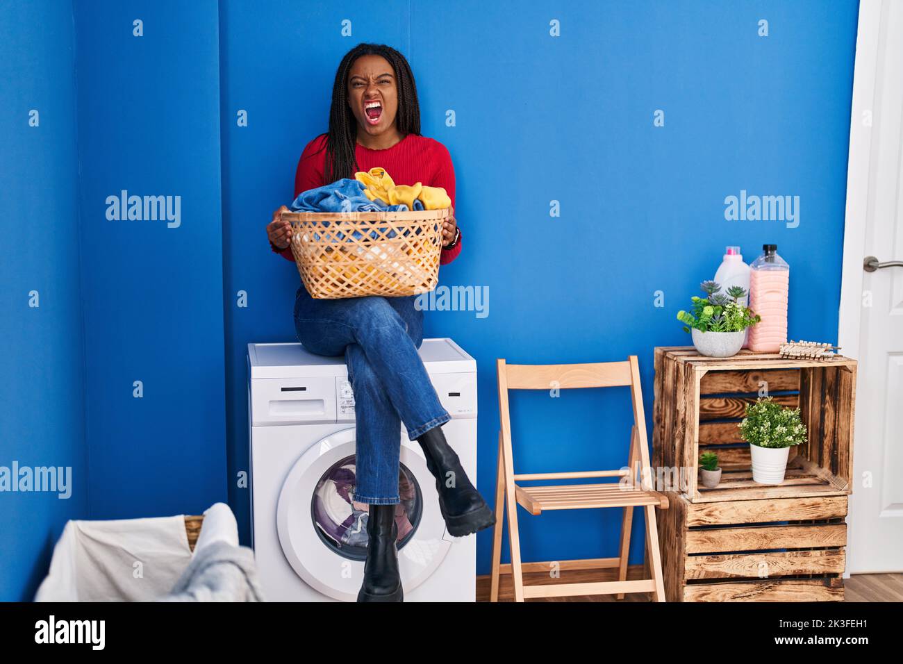 Young african american with braids holding laundry basket sitting on ...