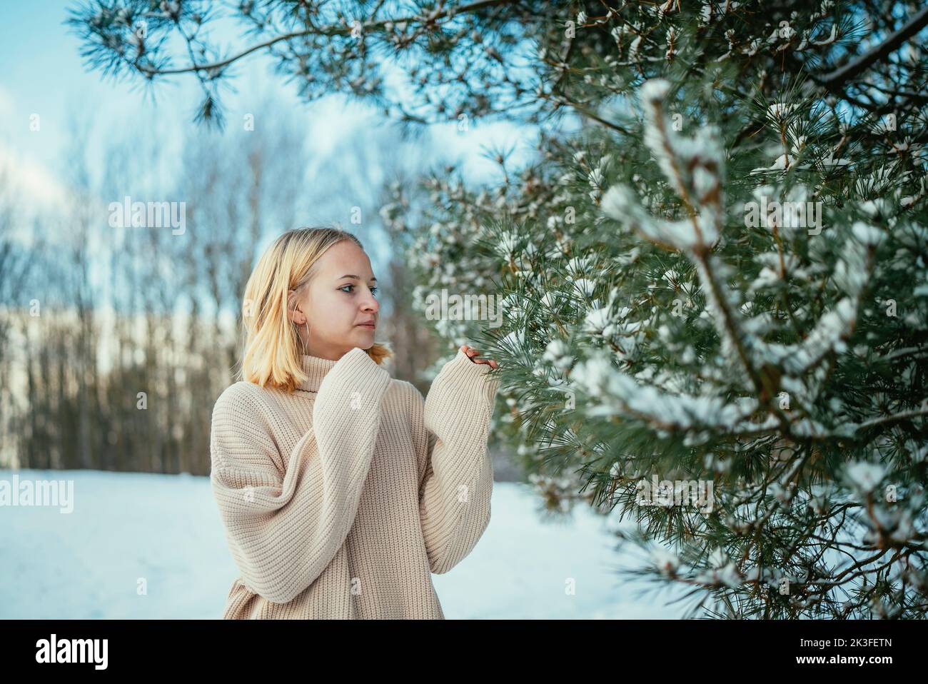 Portrait of a blonde girl in a sweater in a snowy forest on a cold day ...