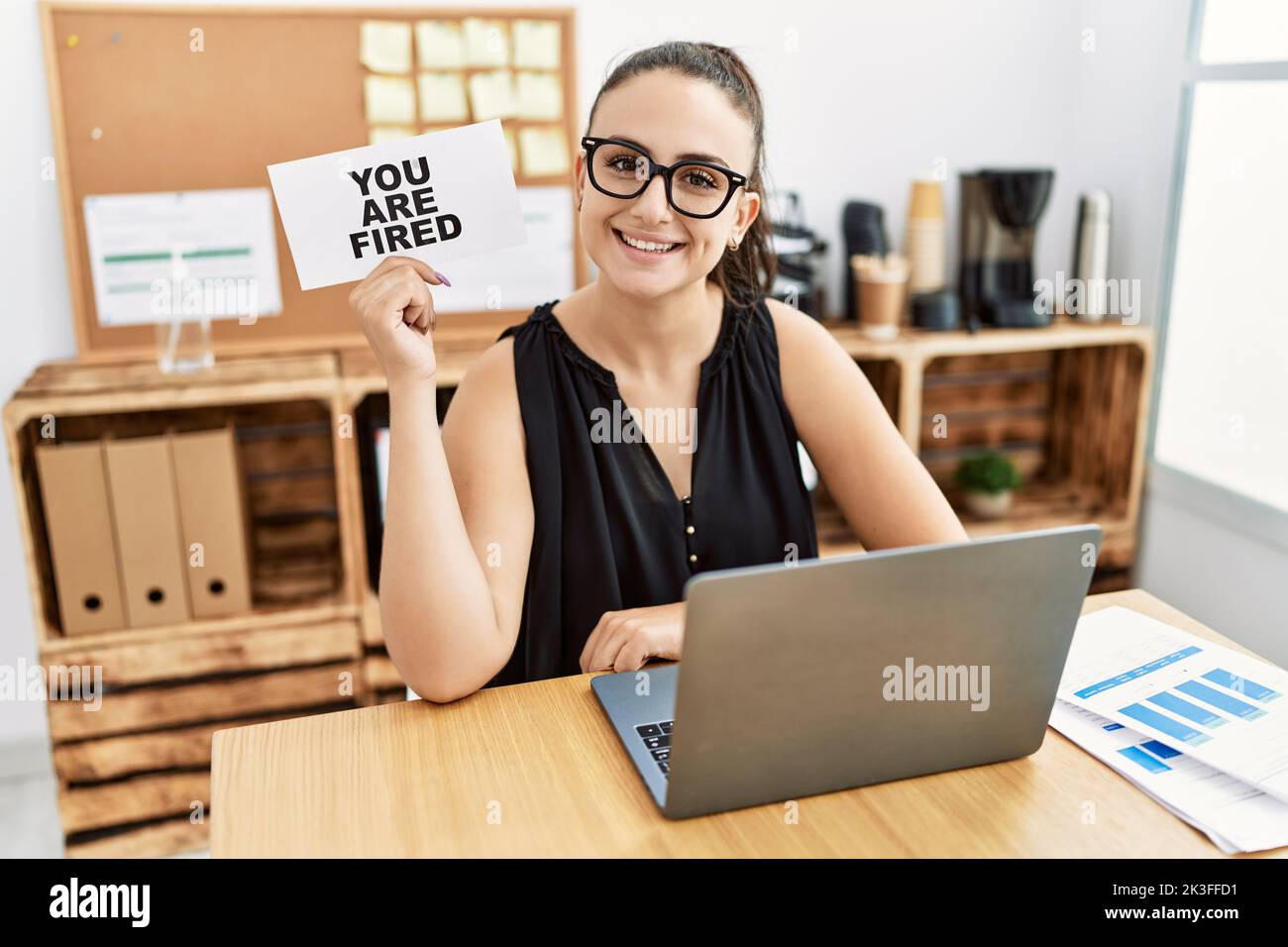 Young brunette woman holding you are fired banner at the office looking ...