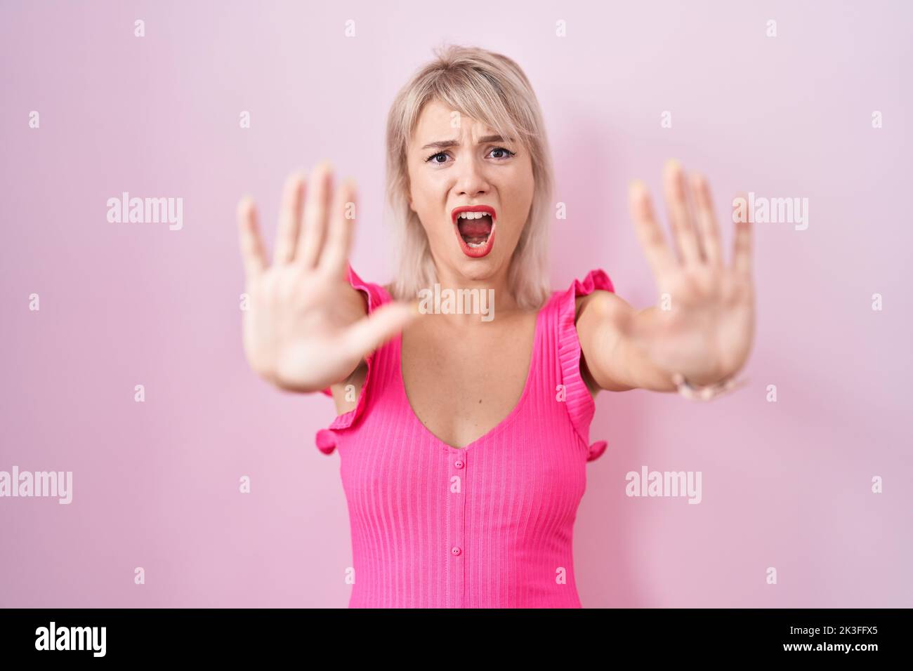 Young caucasian woman standing over pink background doing stop gesture ...
