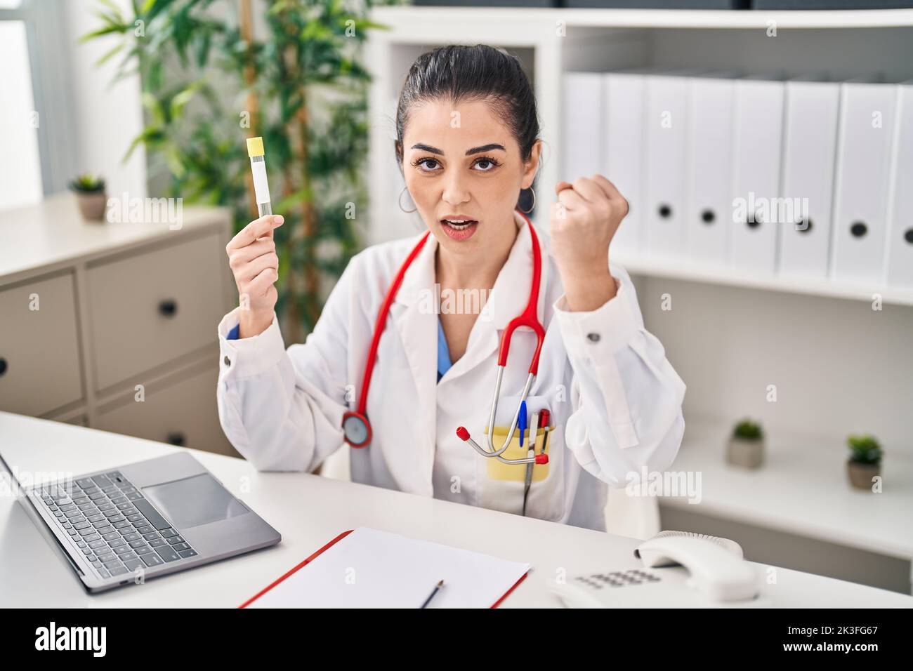 Young doctor woman holding blood sample annoyed and frustrated shouting ...