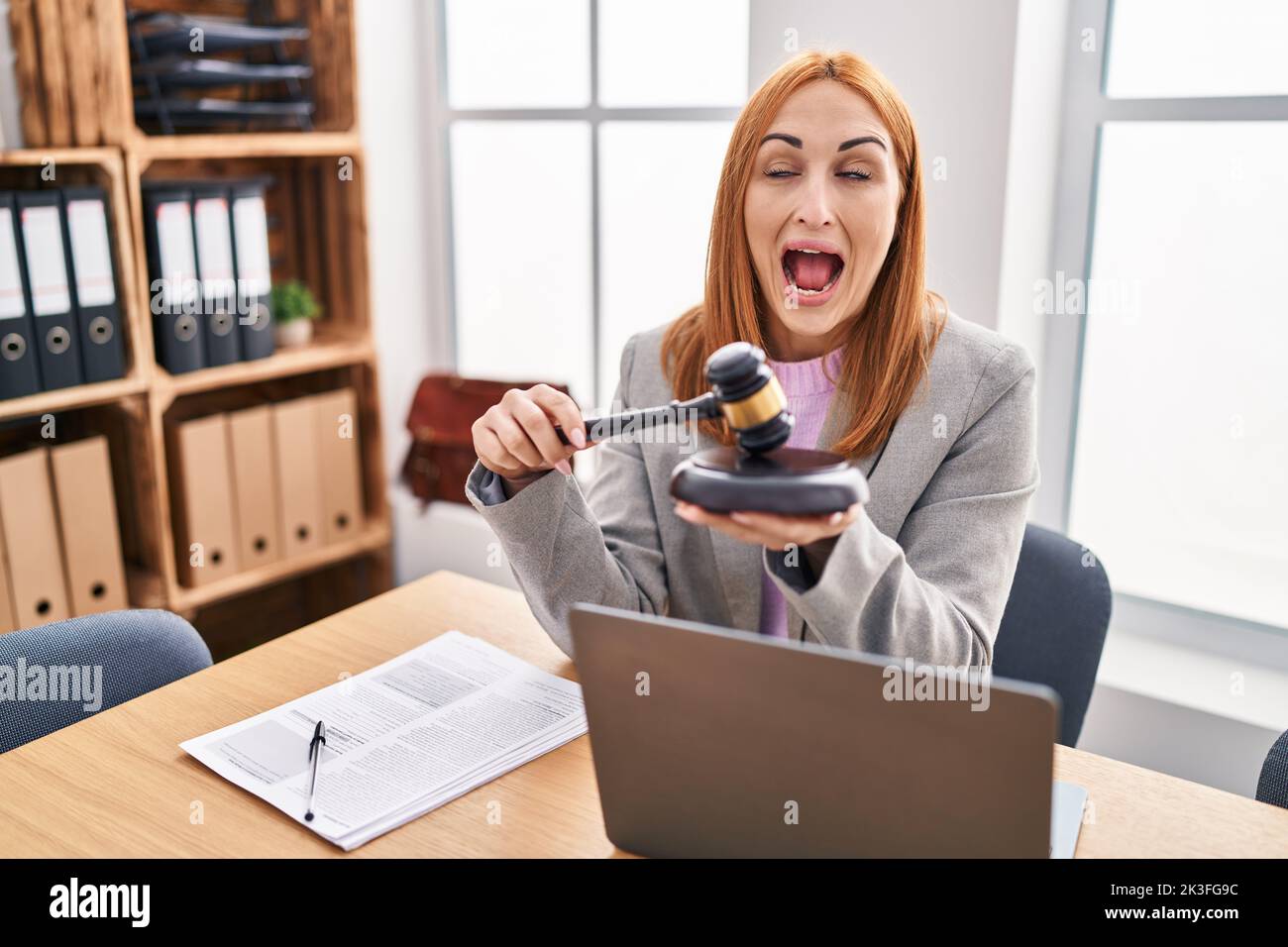Young business woman using gavel angry and mad screaming frustrated and ...