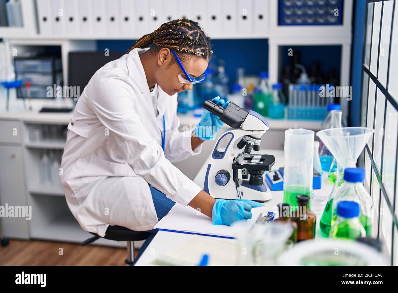 African american woman scientist using microscope writing document at laboratory Stock Photo - Alamy
