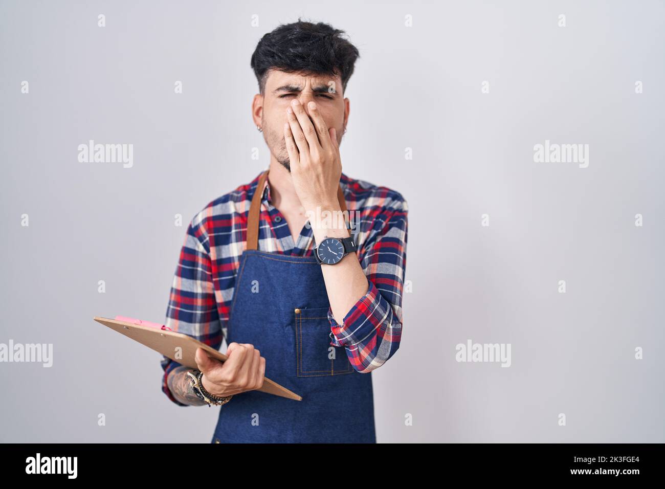 Young hispanic man with beard wearing waiter apron holding clipboard ...