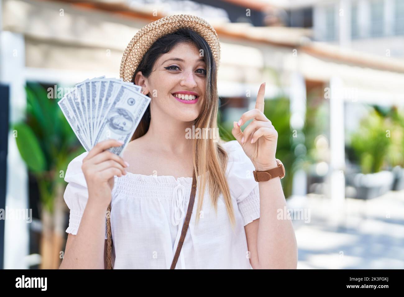 Young brunette woman holding dollars banknotes smiling with an idea or ...