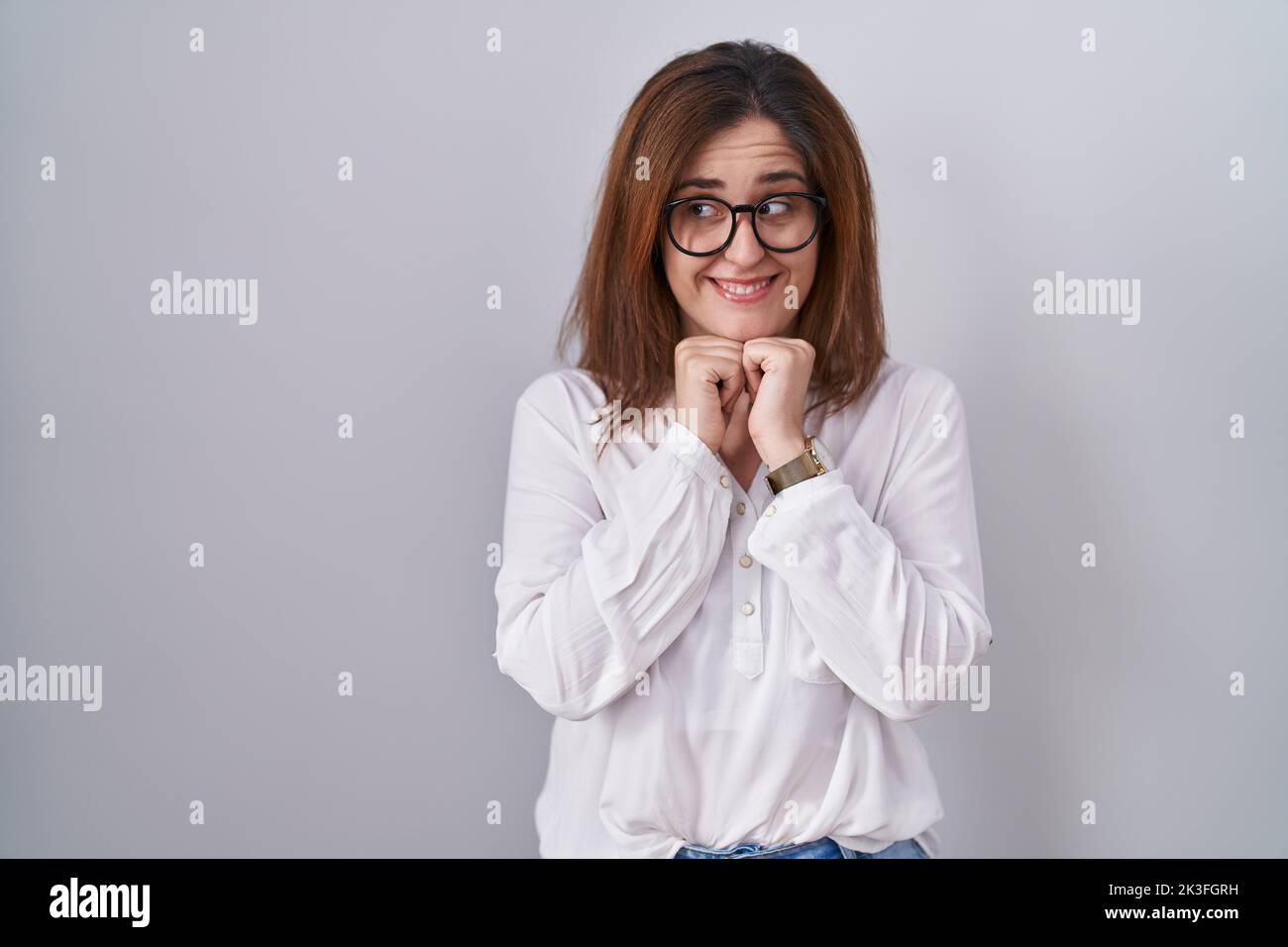 Brunette woman standing over white isolated background laughing nervous ...
