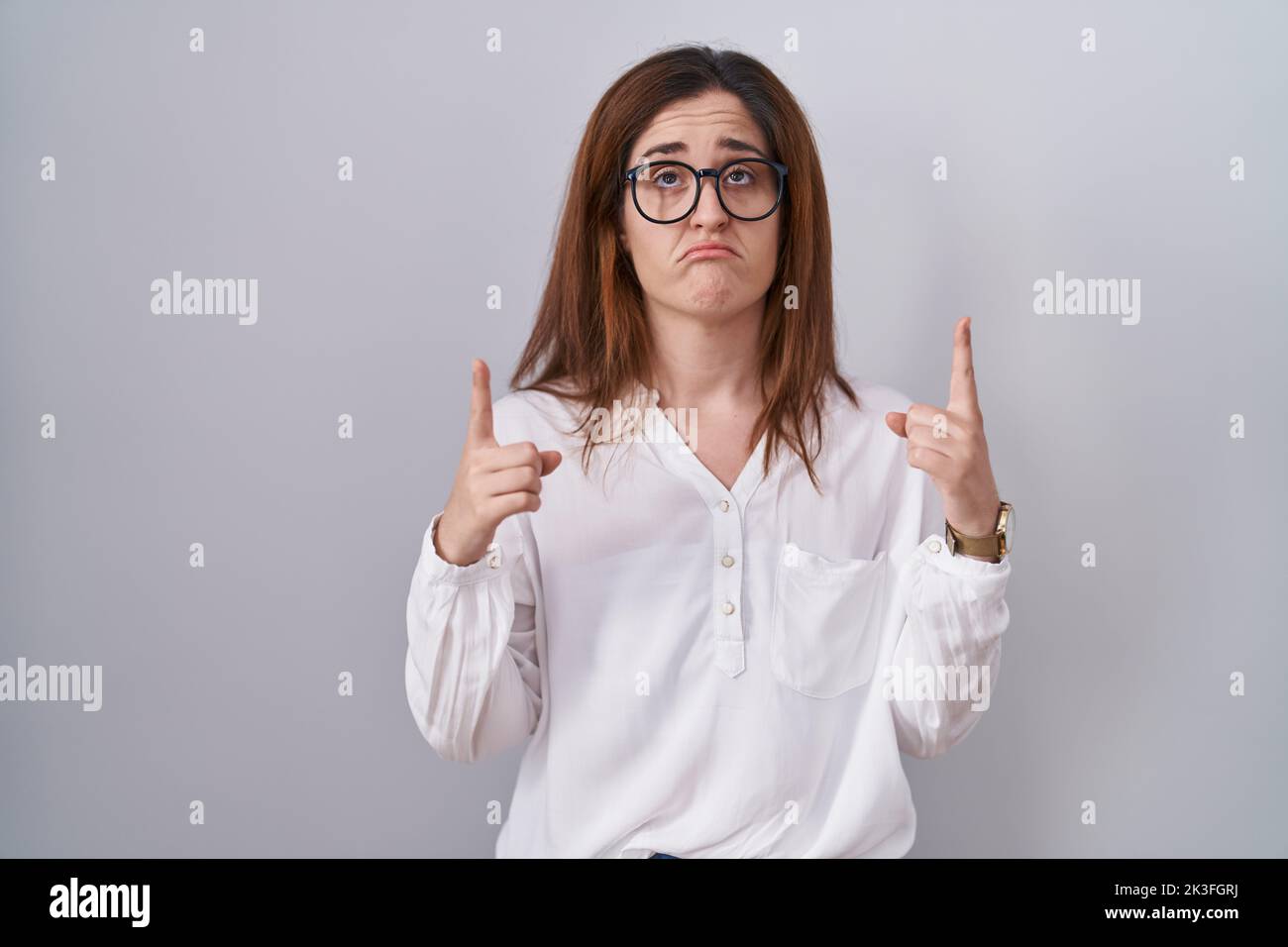 Brunette woman standing over white isolated background pointing up ...