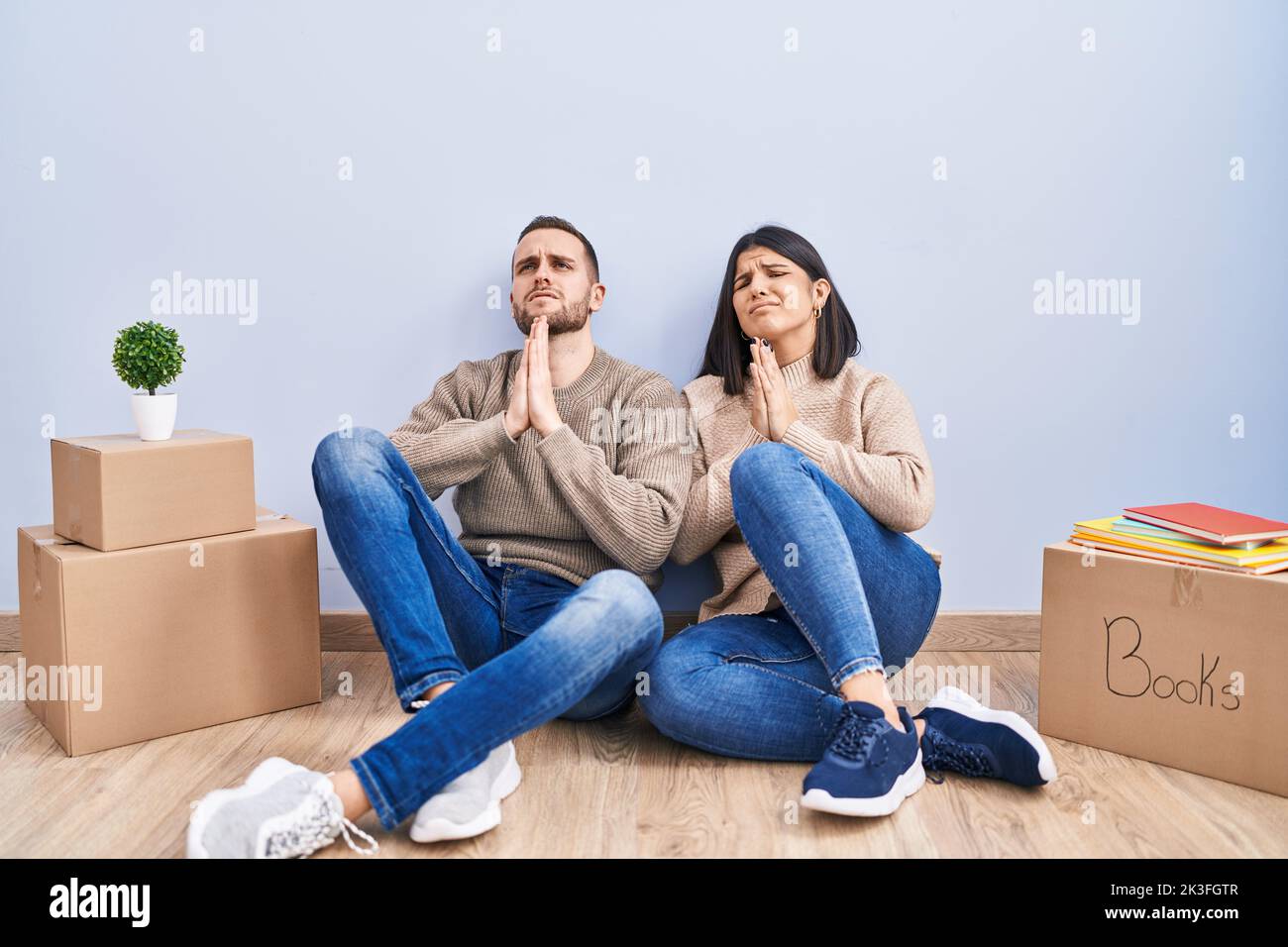 Young couple moving to a new home begging and praying with hands ...