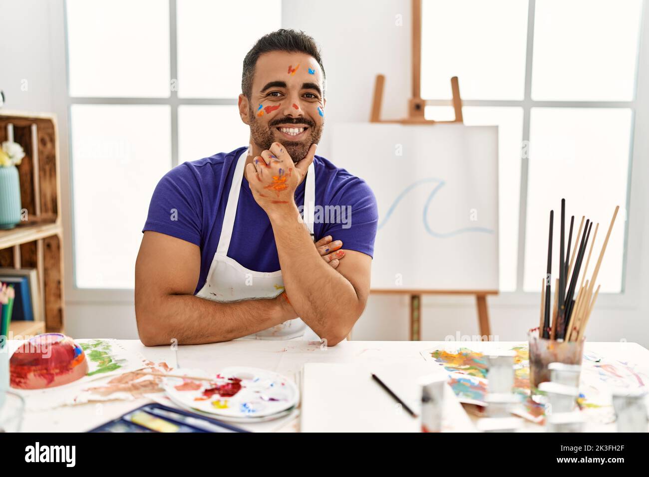 Young hispanic man with beard at art studio with painted face looking ...