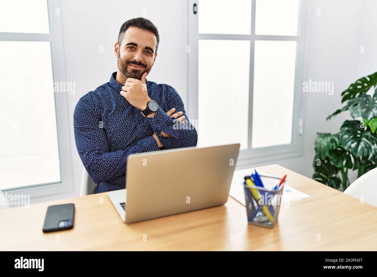 Young hispanic man with beard working at the office with laptop looking ...