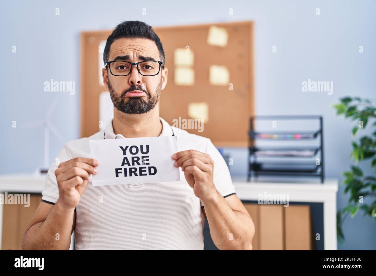 Young hispanic man with beard holding you are fired banner at the ...