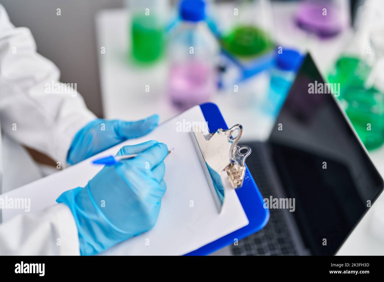 Young hispanic man scientist writing on clipboard at laboratory Stock ...