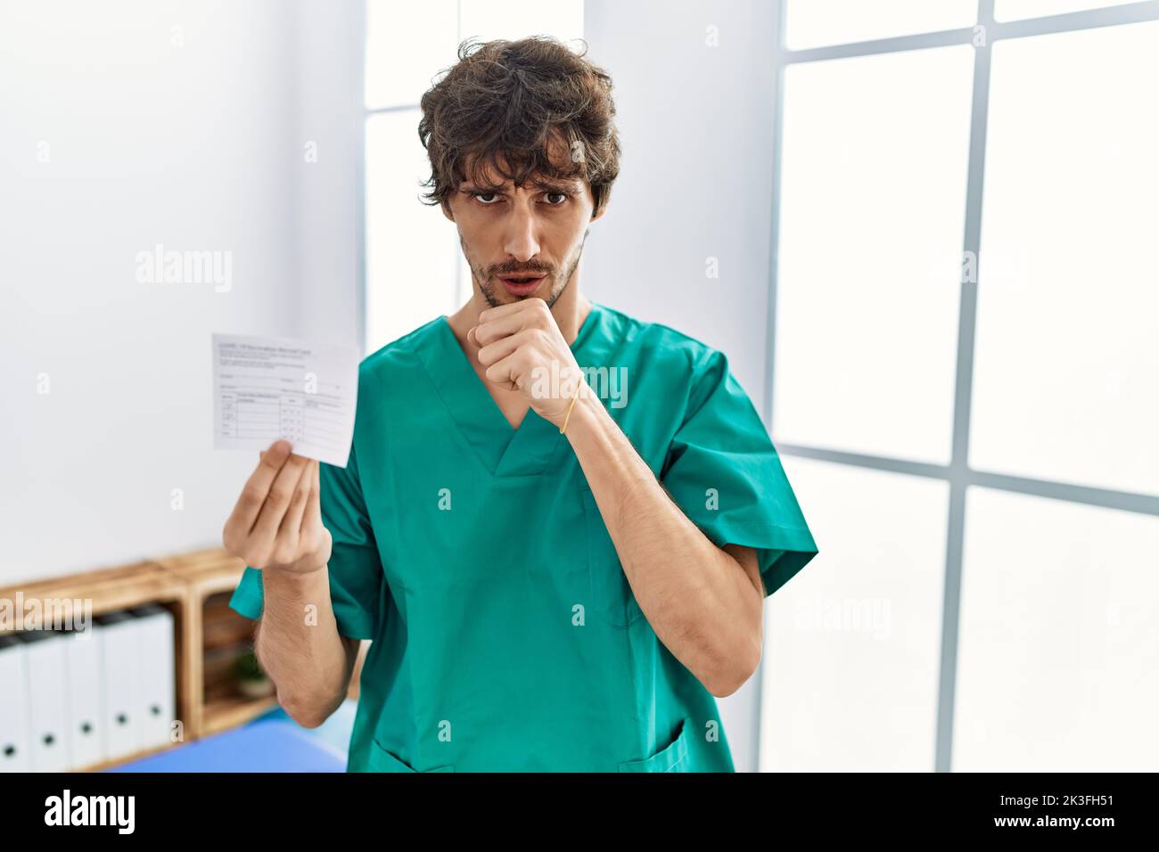 Young hispanic doctor man holding covid record card feeling unwell and ...