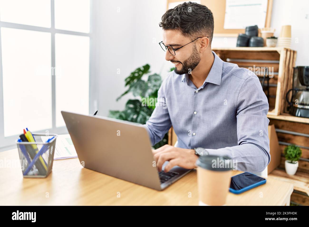 Young arab man smiling confident using laptop and writing on clipboard ...